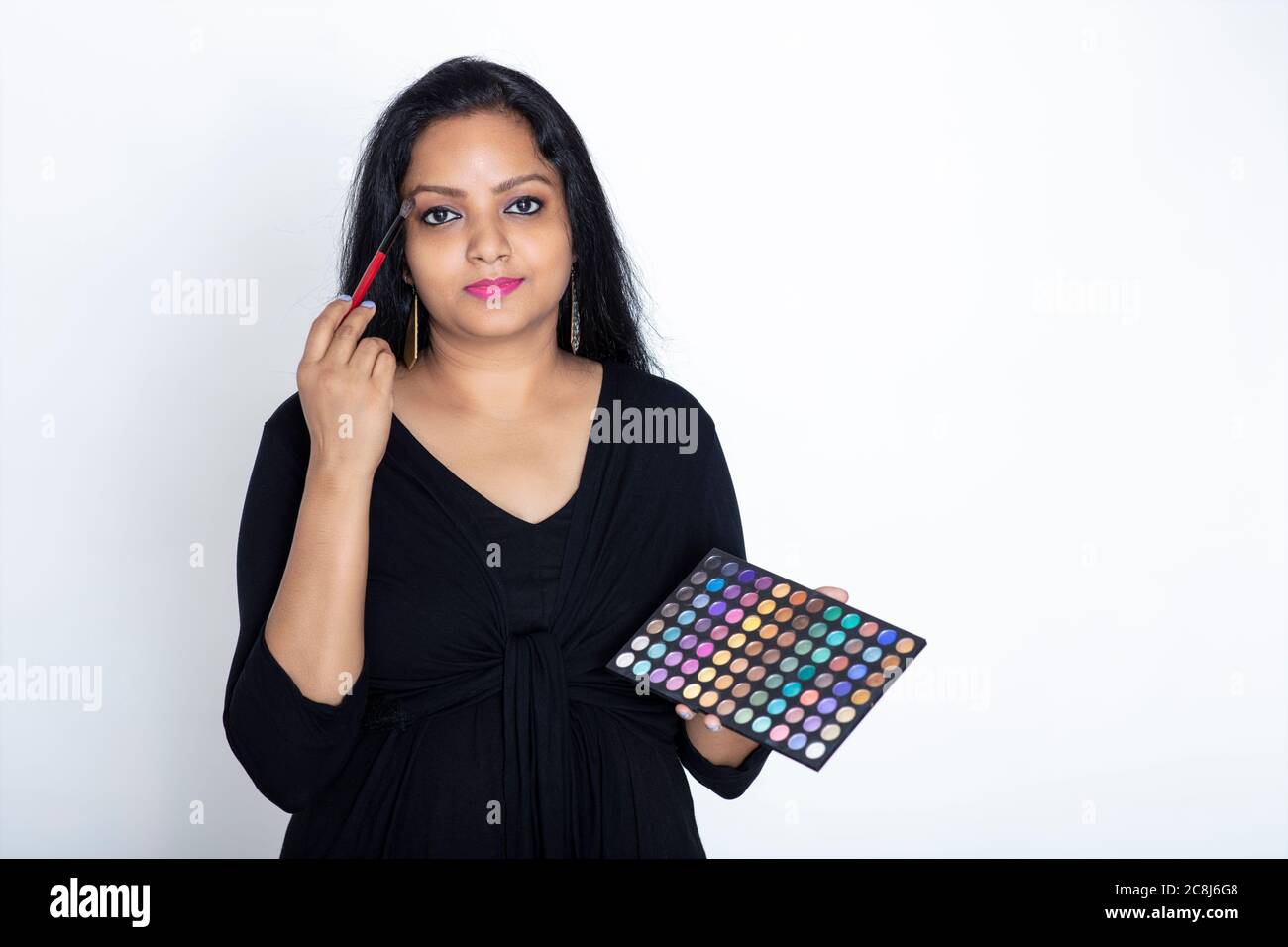 Young attractive Indian female using eye shadow brush and holding ...