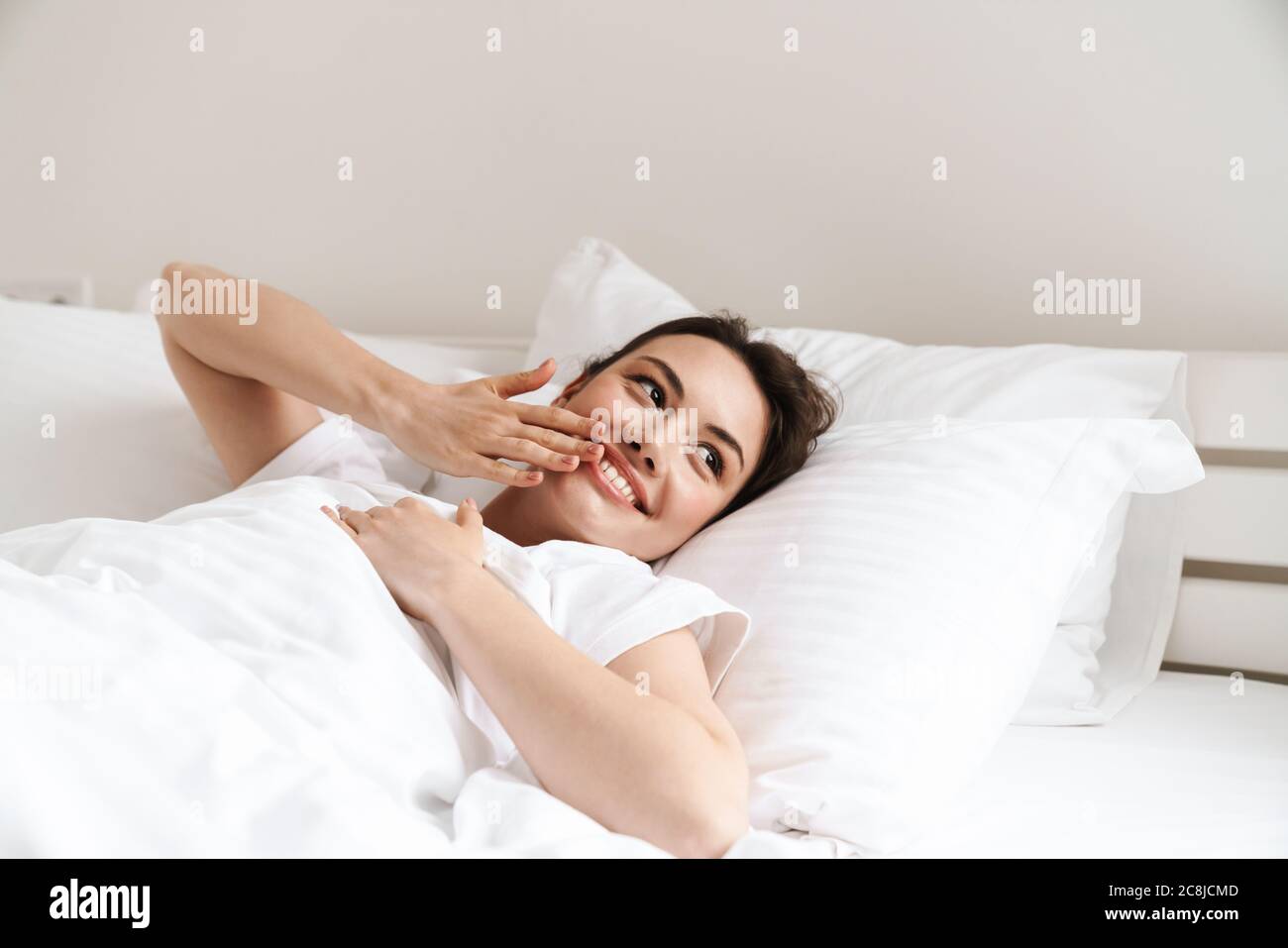 Photo of pretty young cheerful woman laughing while lying on bed after ...