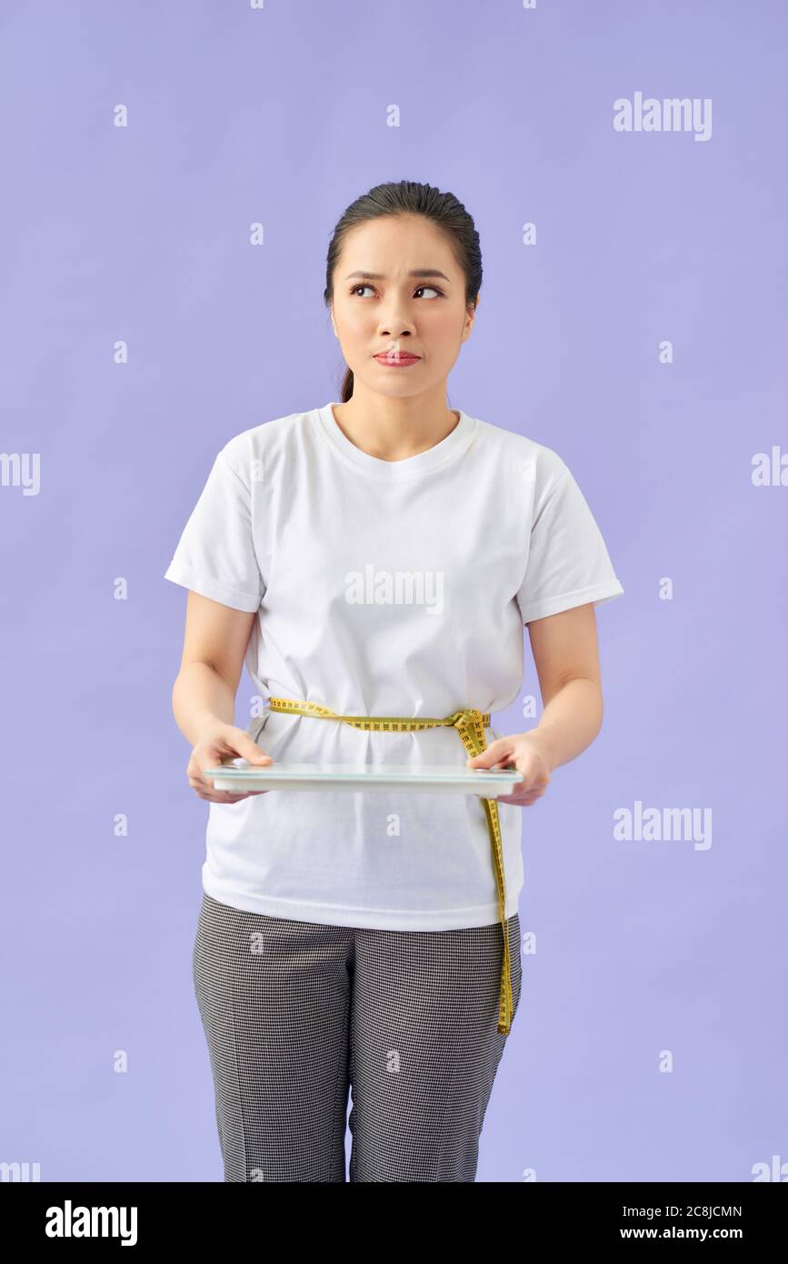 Woman with scale unhappy with her weight gesturing sadness and worry on ...