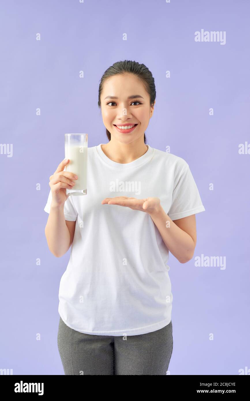 Beautiful asian woman shows a glass of milk, isolated over purple ...