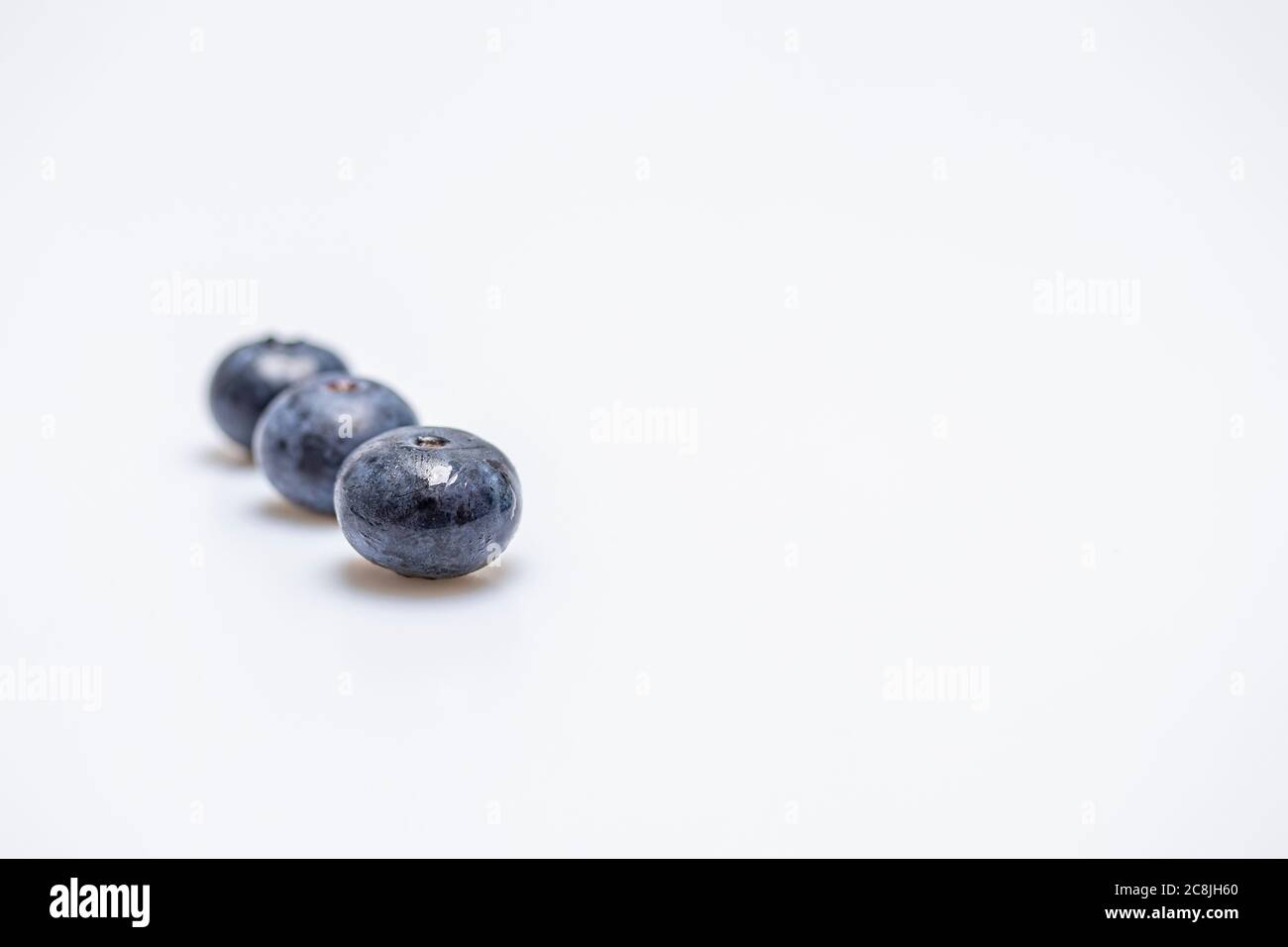 Three blueberries in a row on white background Stock Photo - Alamy