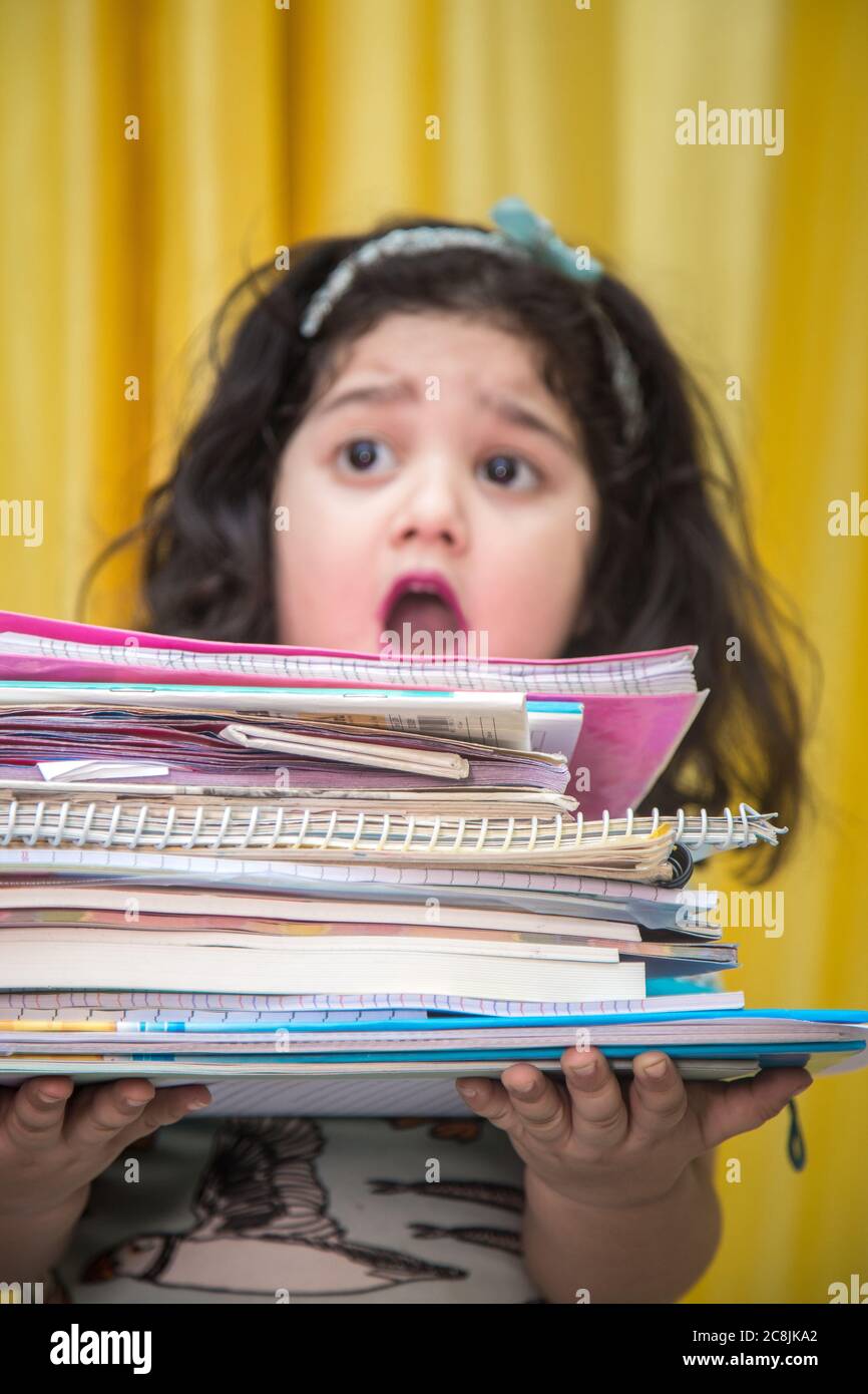 Close up of sad little schoolgirl with a stack of heavy books ...