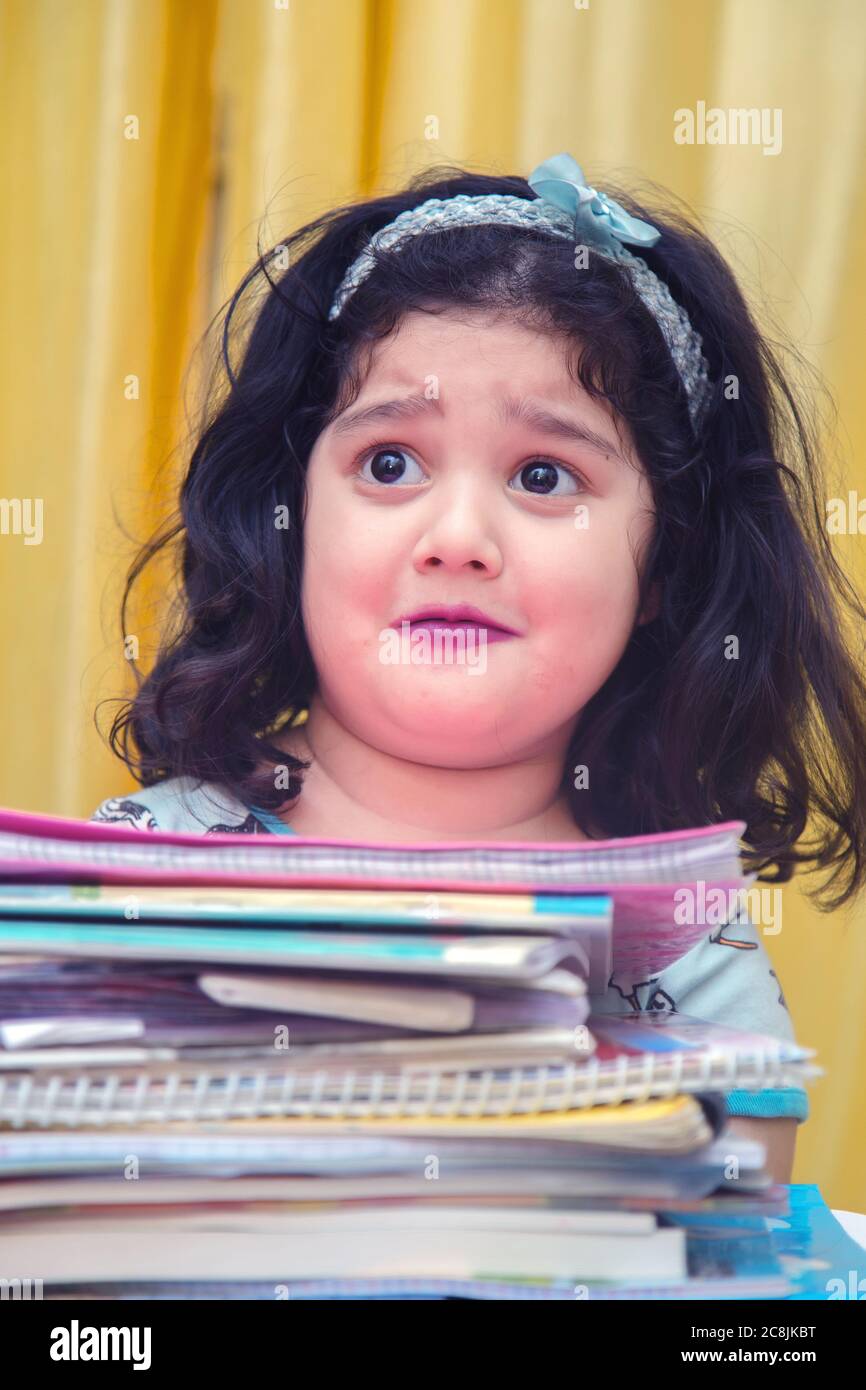 Close up of sad little schoolgirl with a stack of heavy books ...