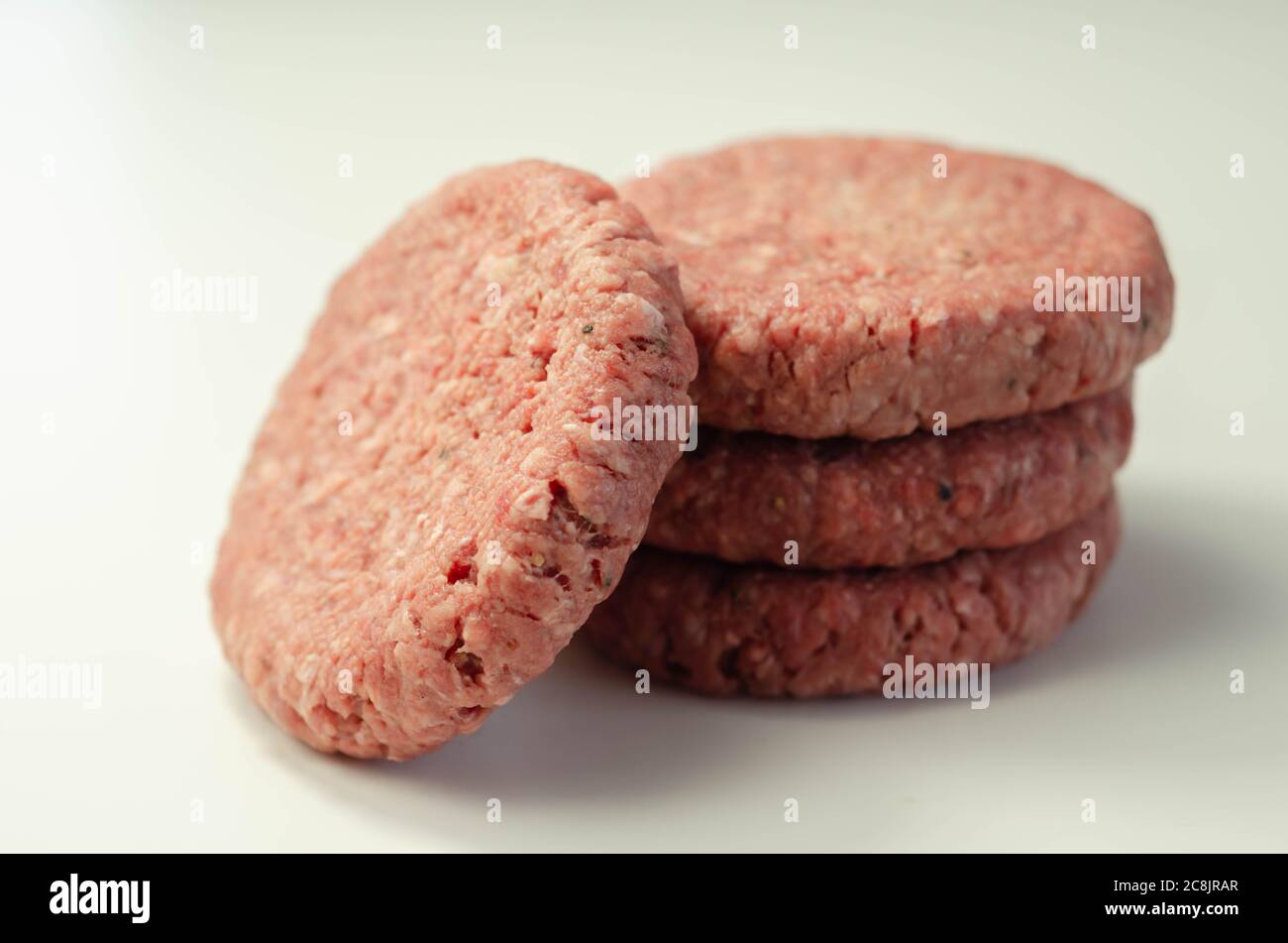 Raw beef burgers with a pinch of salt and black pepper on the white ...