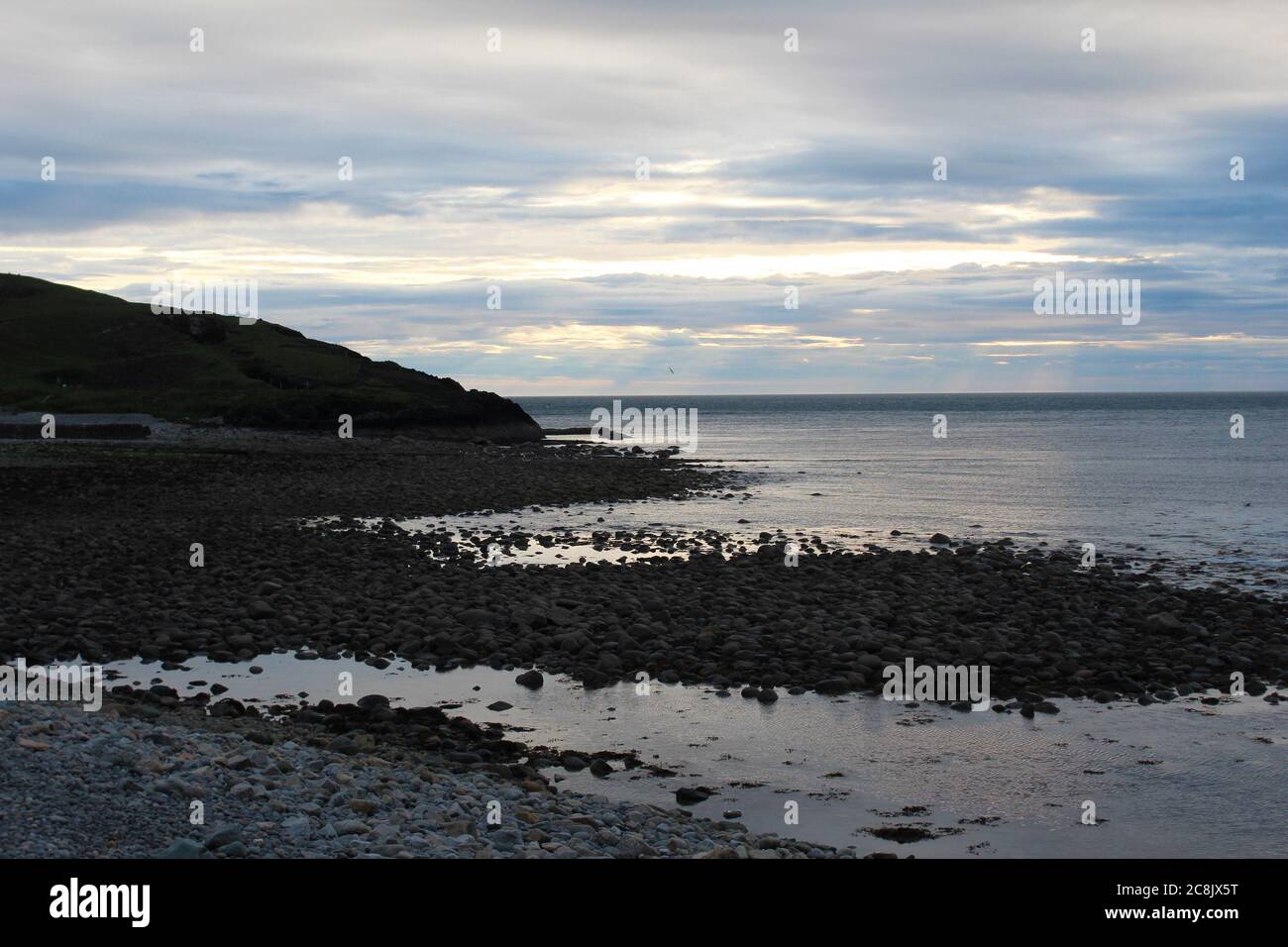 Sun rays coming through clouds onto the ocean, seen from a rocky beach ...