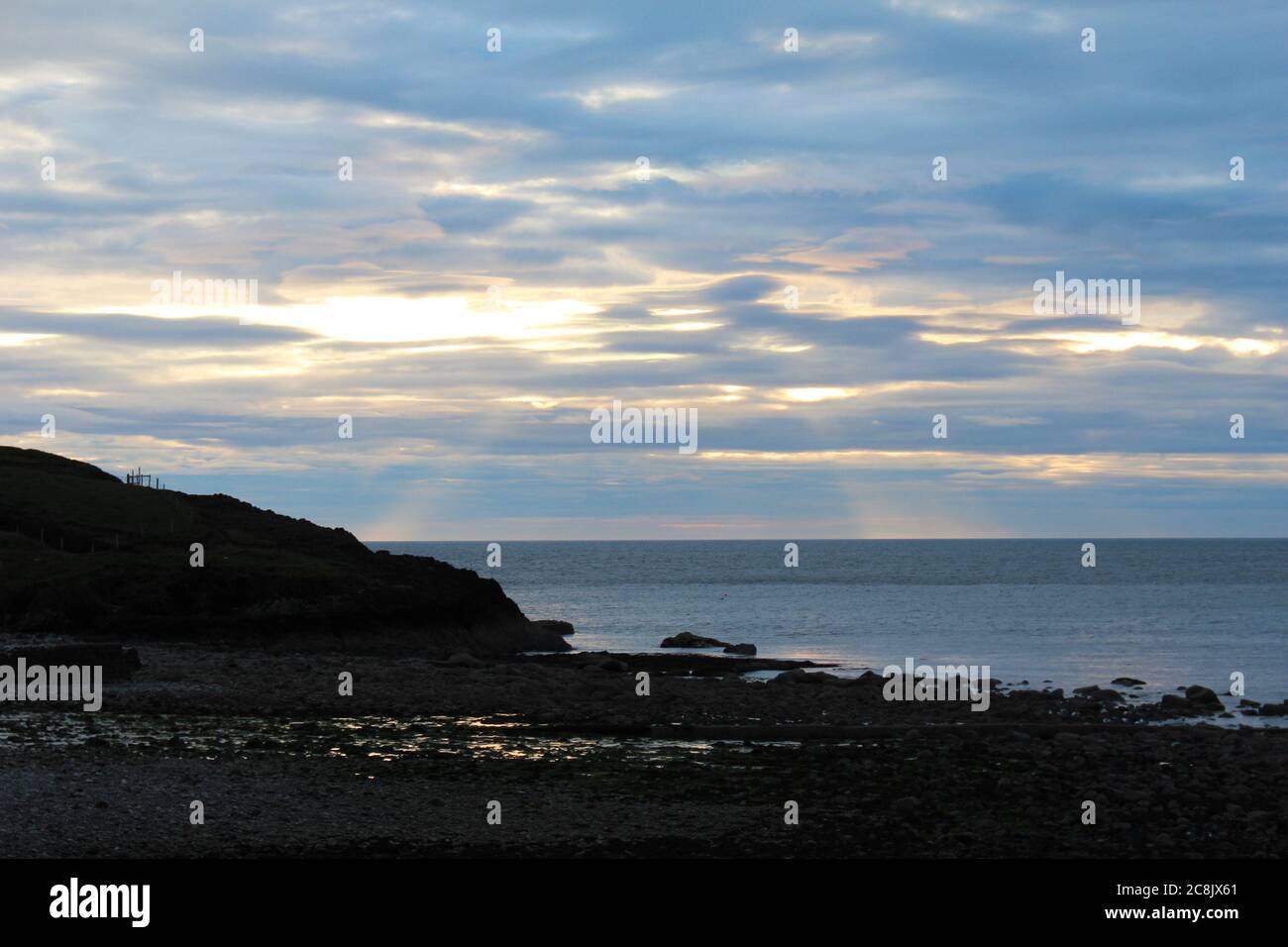 Sun rays coming through clouds onto the ocean, seen from a rocky beach ...