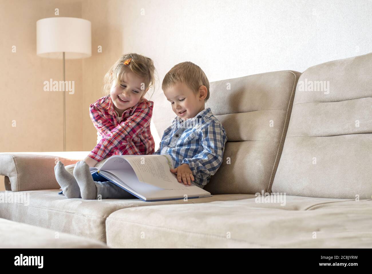 Cute little brother and sister reading a book together on the couch at ...