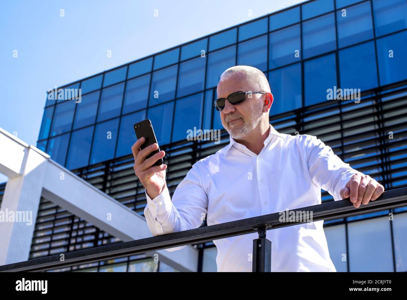 Businessman leaning on the balcony railing in front of an office ...