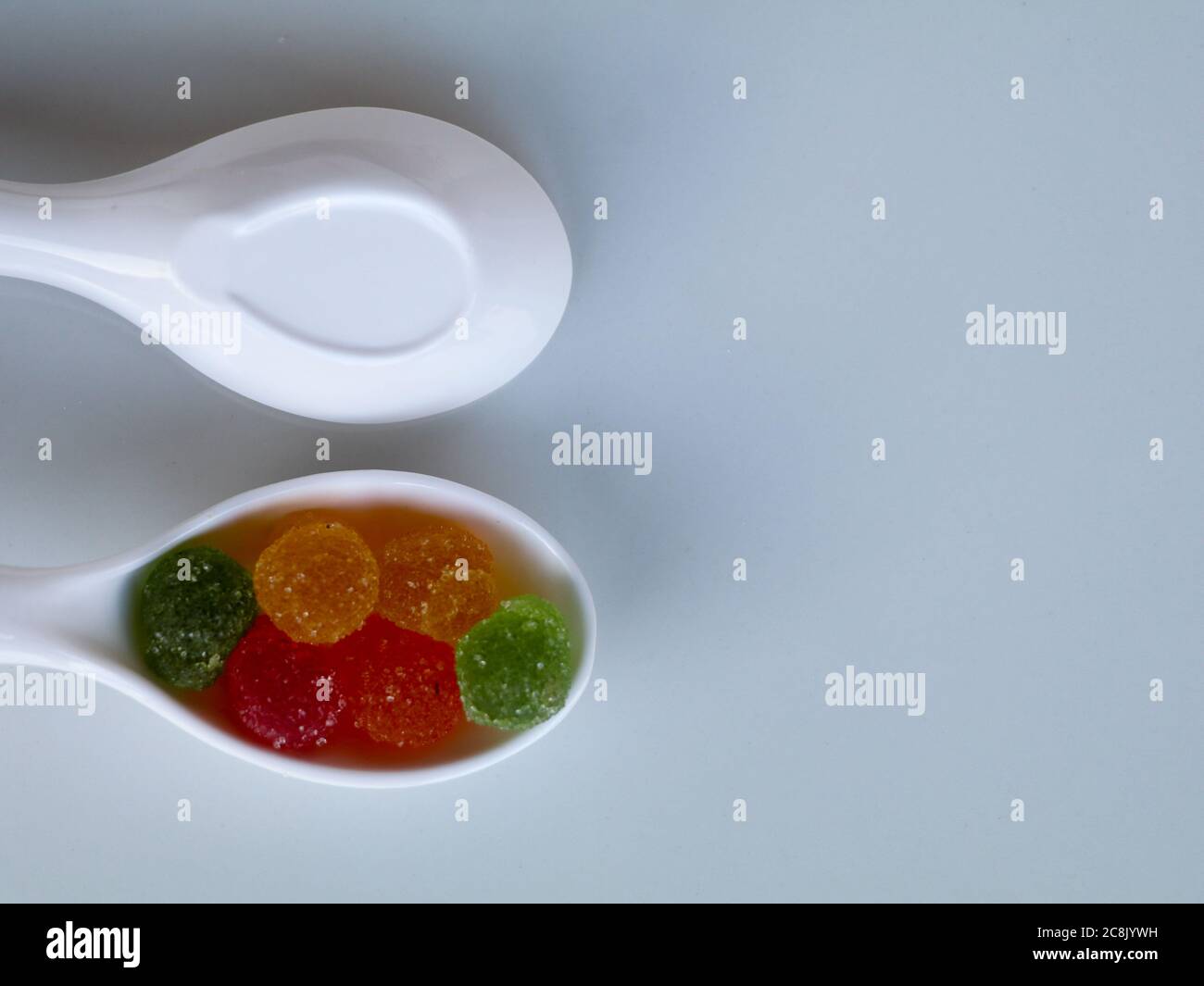 Sweet mixed color jelly candy in a white spoon against white background ...