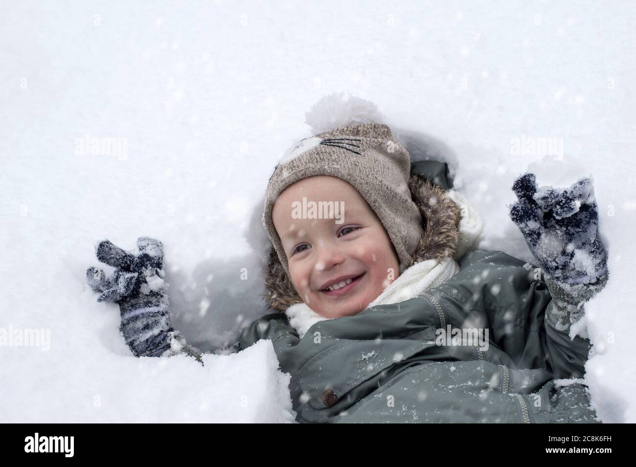 Little happy Caucasian boy lying on his back in the snow and enjoying ...