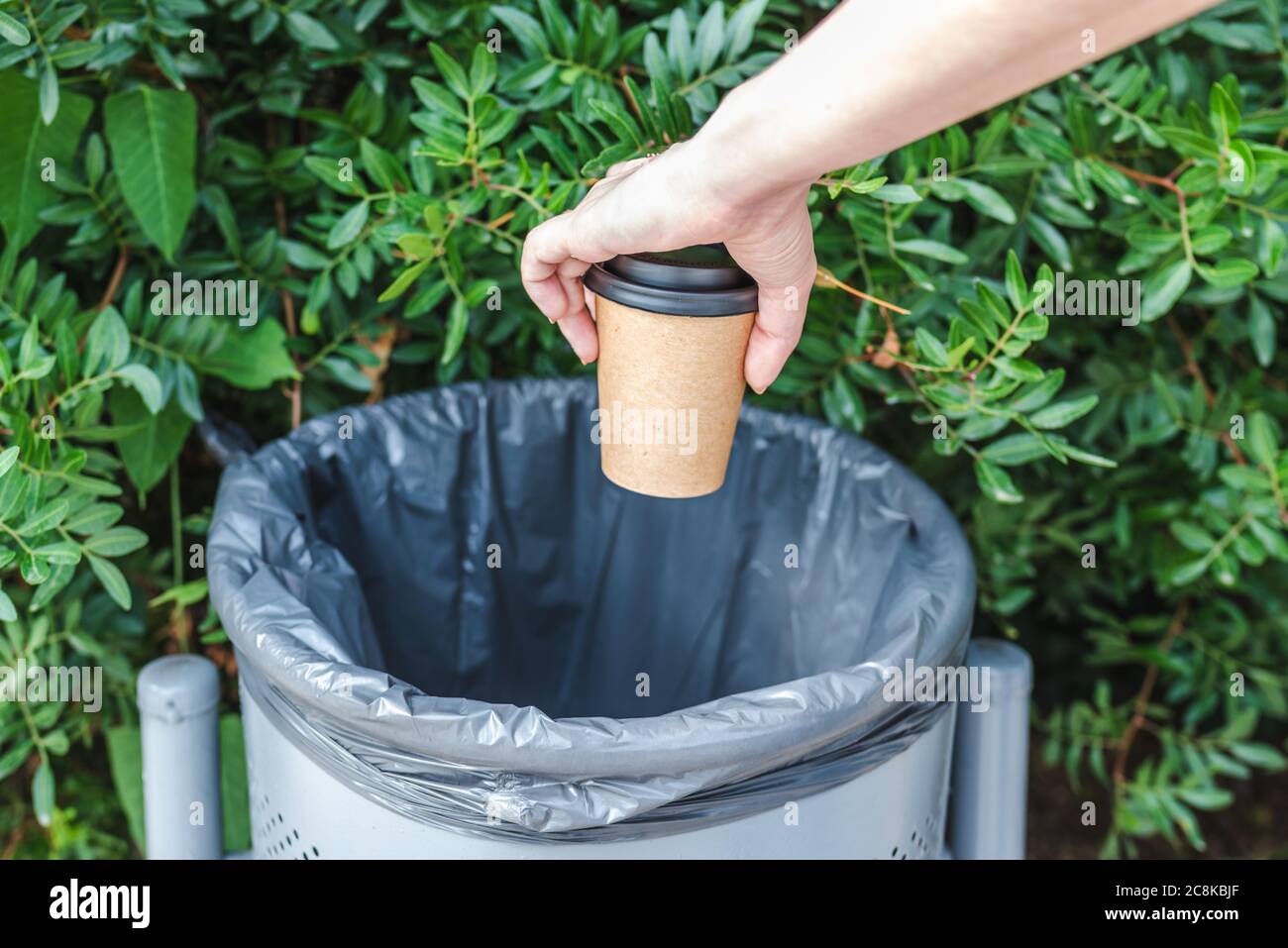 hand of a caucasian woman trashing a cup of take away coffee in a bin ...