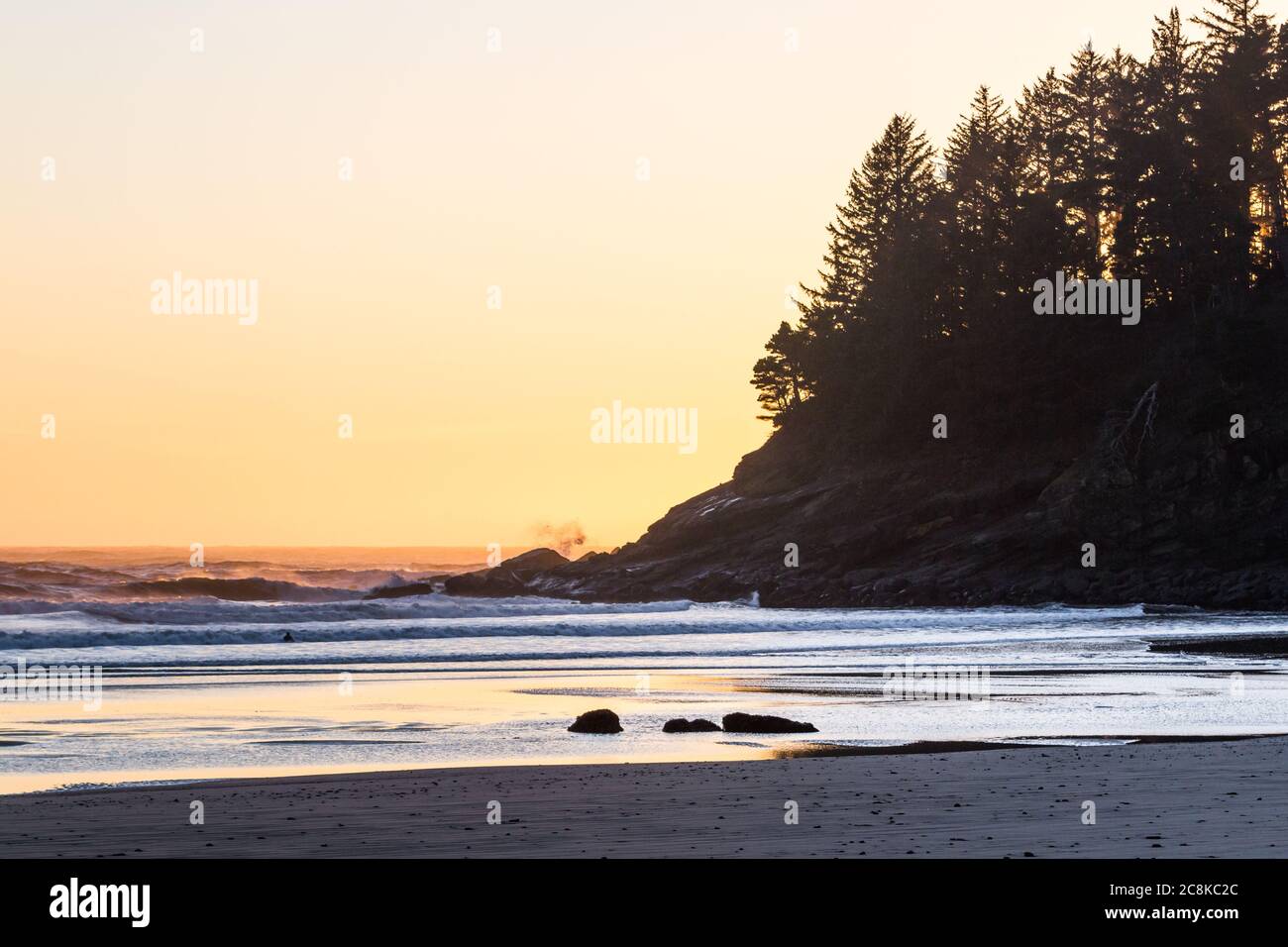 Man in the cold coastal waters of the Oregon coast surfing at sundown ...