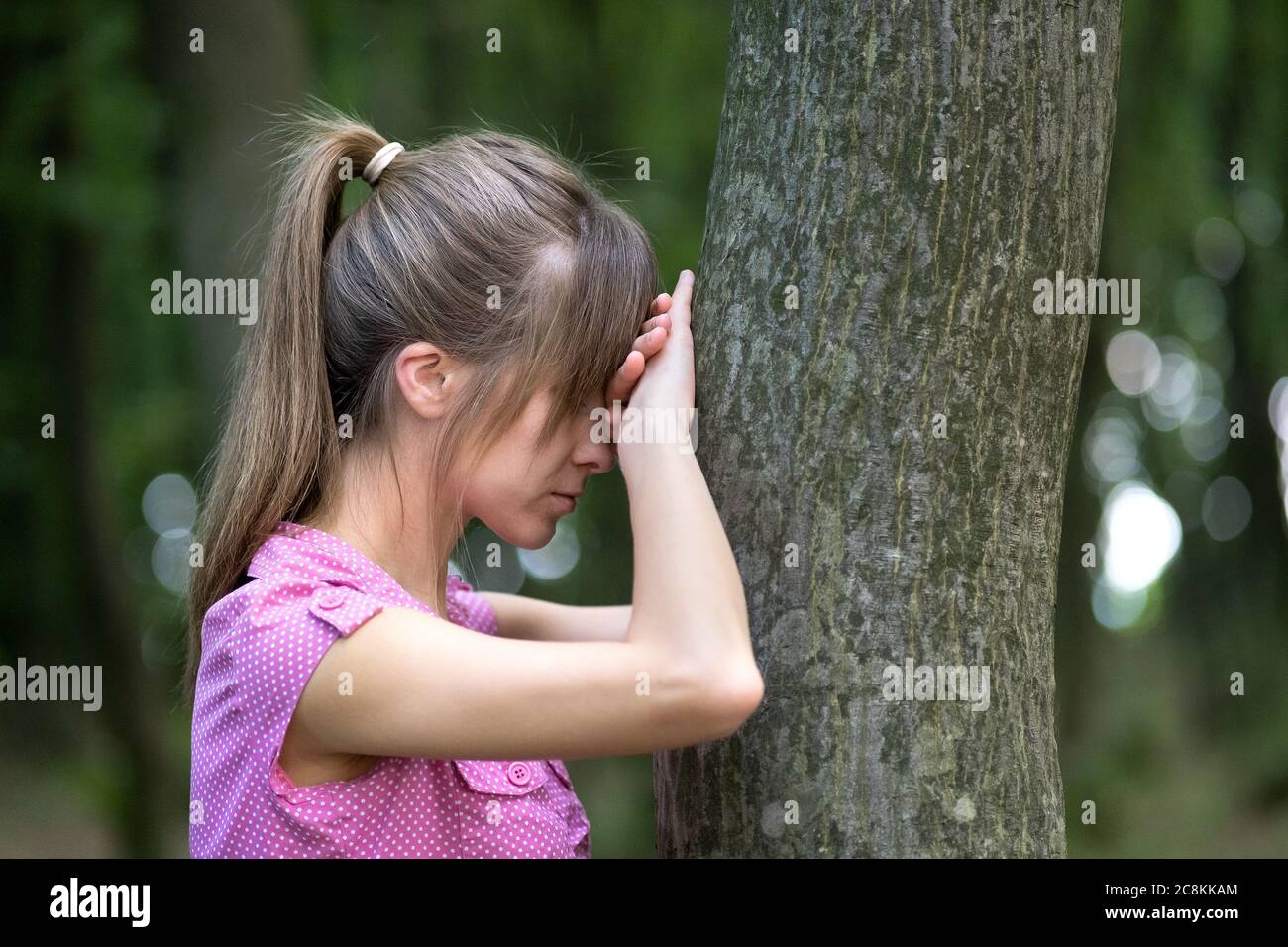 Young tired woman leaning to tree trunk in summer forest Stock Photo ...