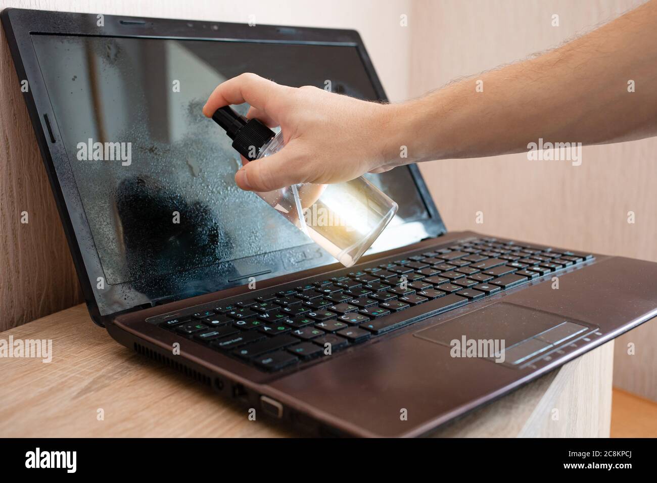 The man cleans the laptop from dust and bacteria with alcohol spray ...