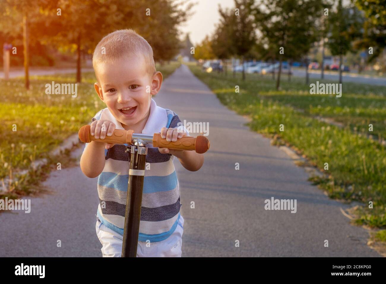 Picture of a happy kid riding a scooter in a park Stock Photo - Alamy