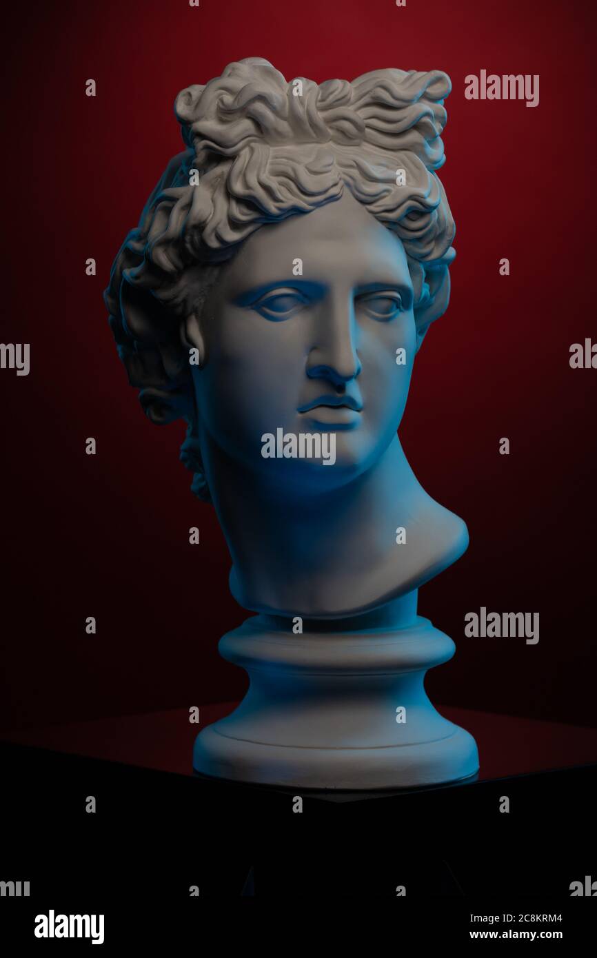 Statue of a bust of Apollo's head in blue local light on a dark red ...