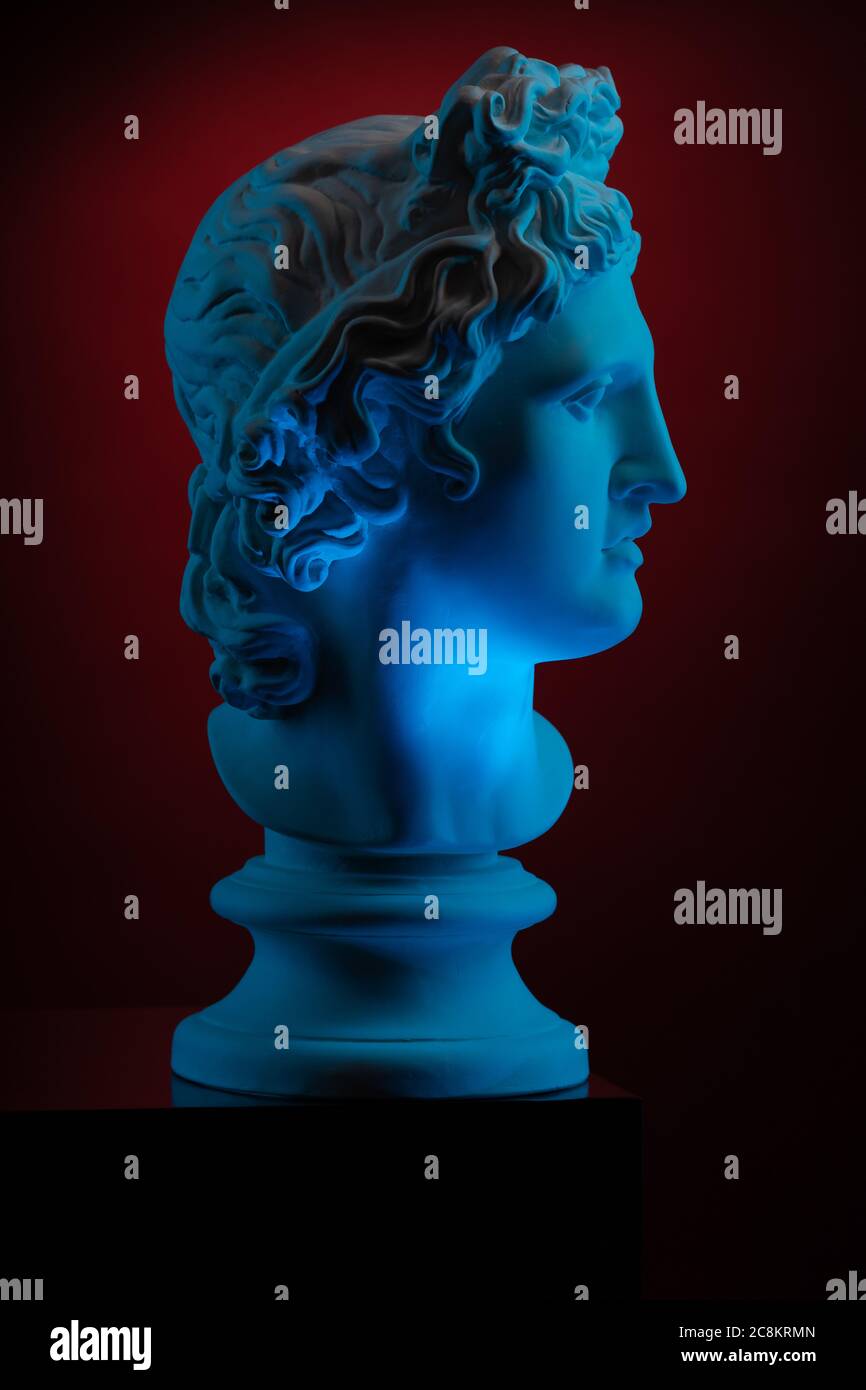 Statue of a bust of Apollo's head in blue local light on a dark red ...