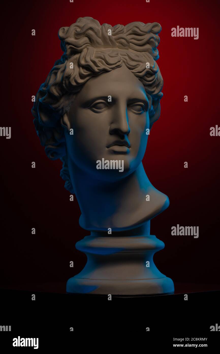 Statue of a bust of Apollo's head in blue local light on a dark red ...