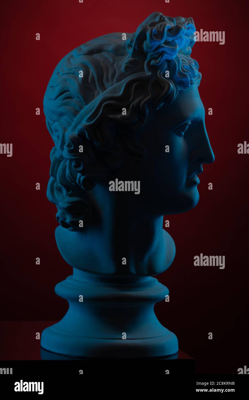 Statue of a bust of Apollo's head in blue local light on a dark red ...