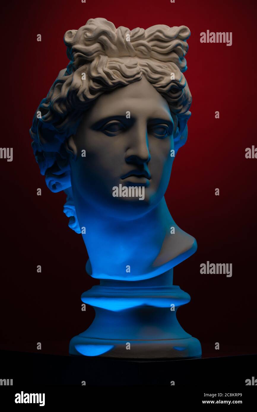 Statue of a bust of Apollo's head in blue local light on a dark red ...