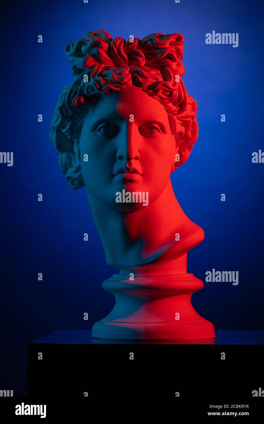 Plaster statue bust of Apollo Belvedere in red and blue light on a blue ...