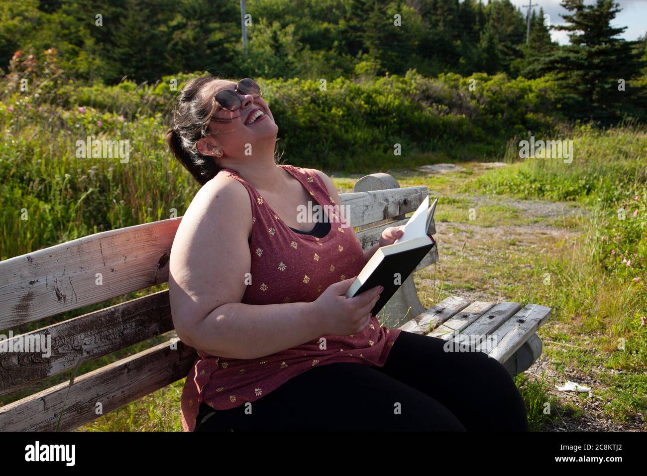 Woman chuckles while reading her book outside on a park bench Stock ...