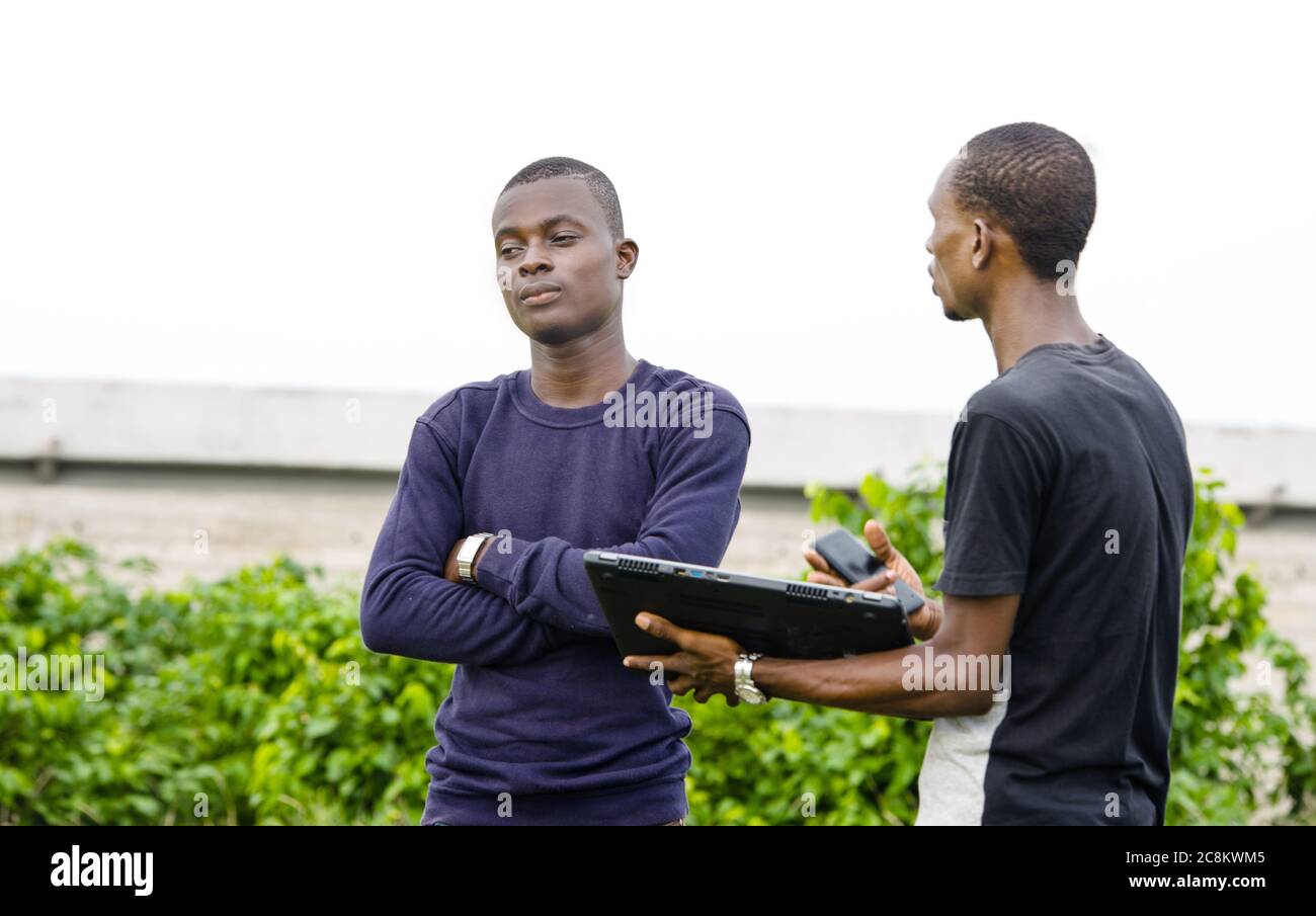 Young people standing with one laptop and talking to each other Stock ...