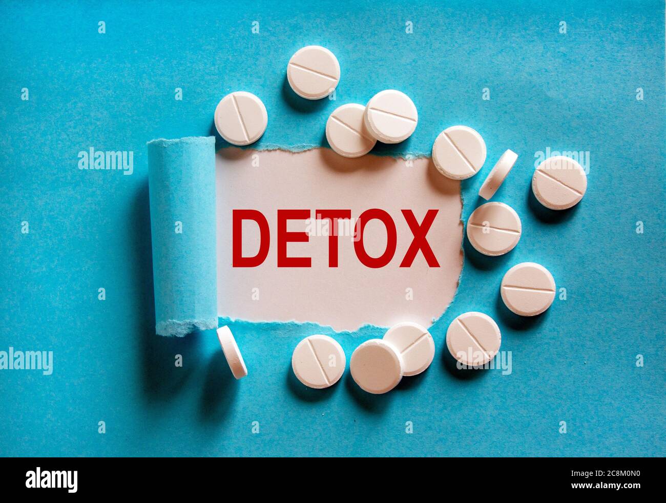 The word 'detox' appearing behind torn blue paper. White pills ...