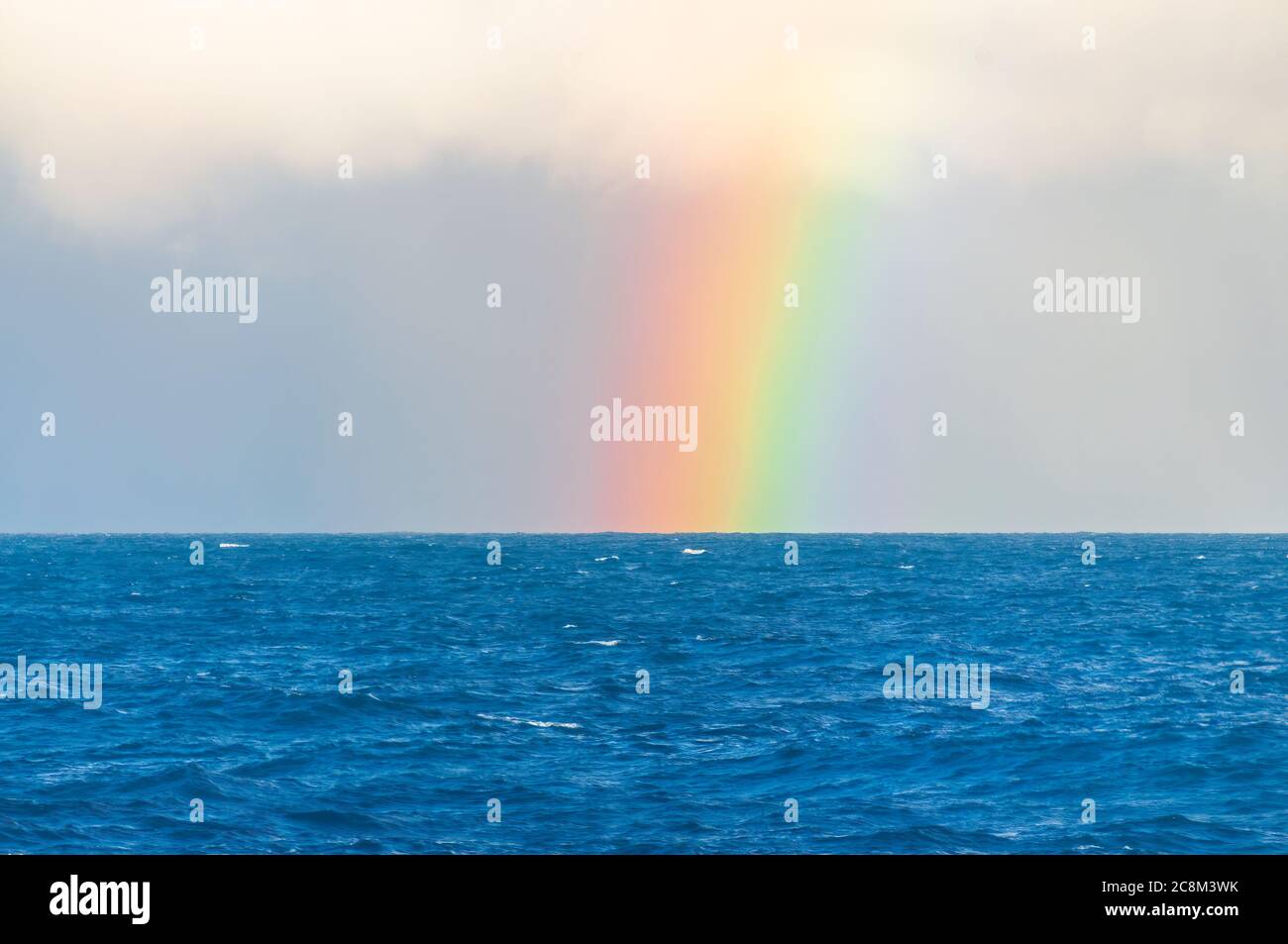 Colorful vertical rainbow over a tranquil sea with blue sky and a cloud ...