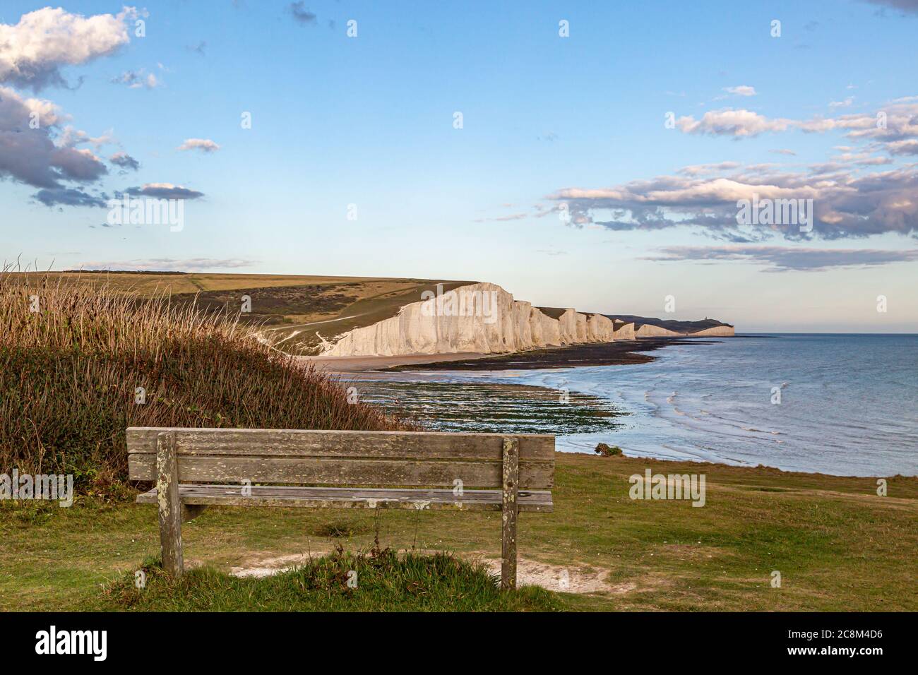 A bench on a cliff with a view of the Seven Sisters, with evening light ...