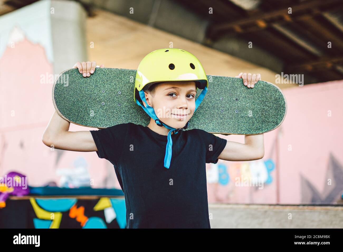 Caucasian child skateboarder posing with skate board on shoulders an ...