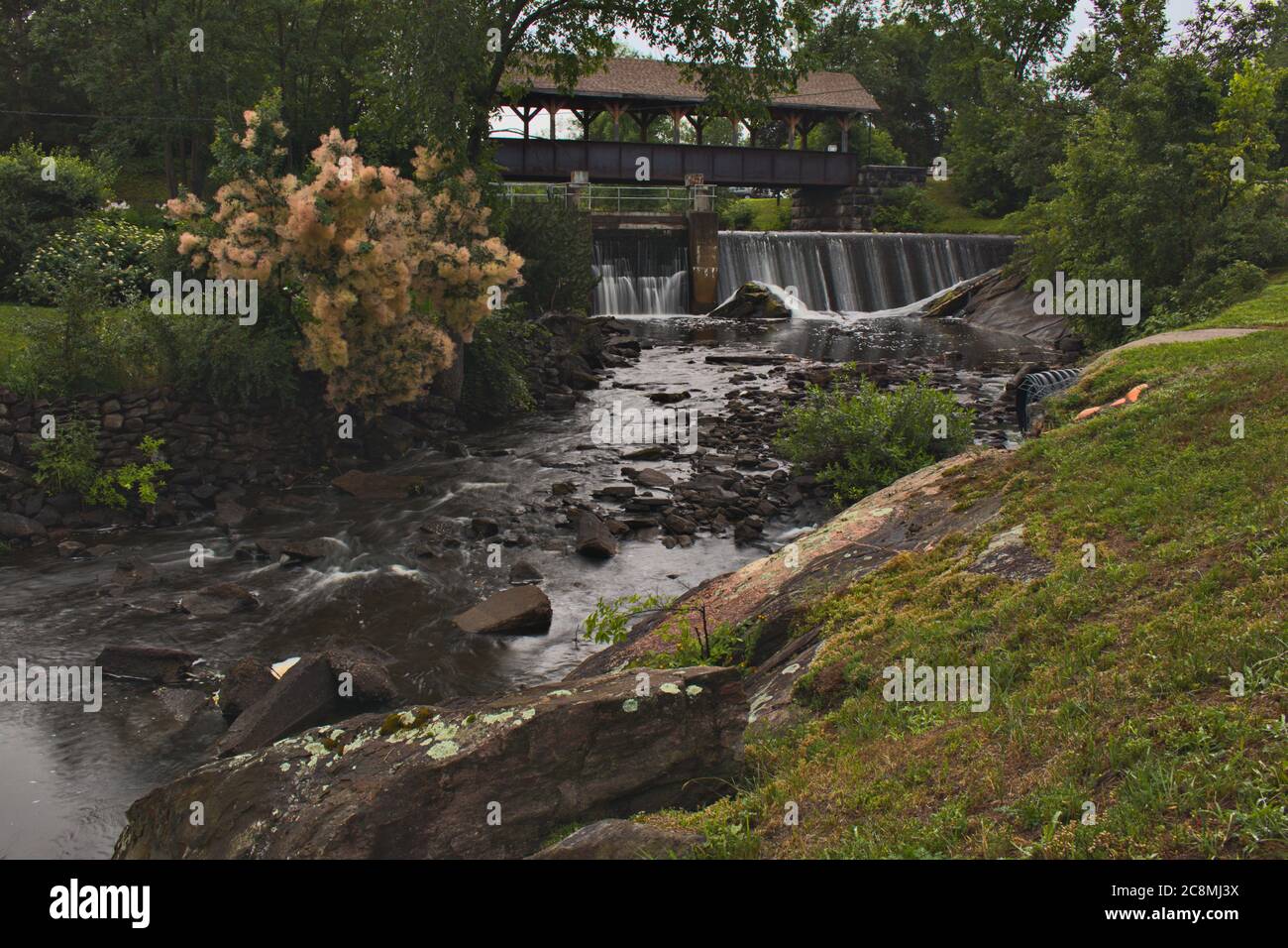 covered bridge with a small waterfall underneath, leading to a river ...