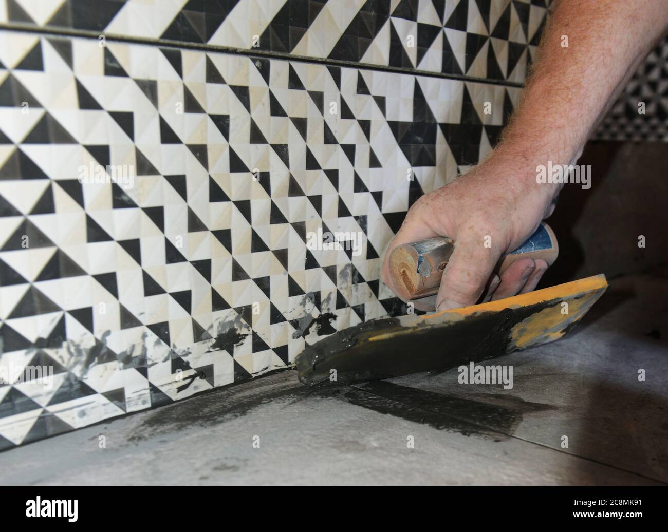 The hand of man holding a rubber float and filling joints with grout ...