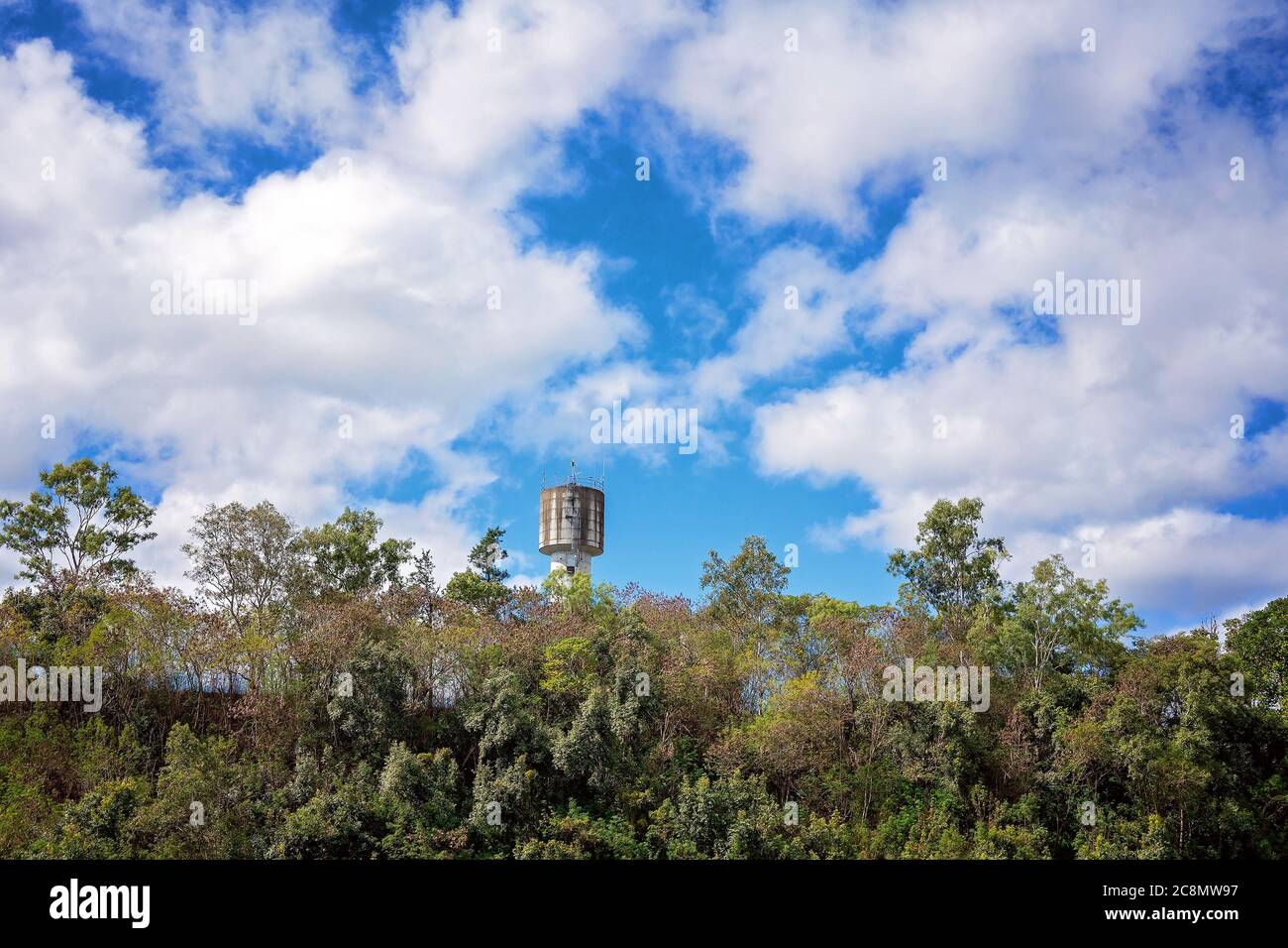 Concrete water tower with a forest foreground and cloudy blue sky ...