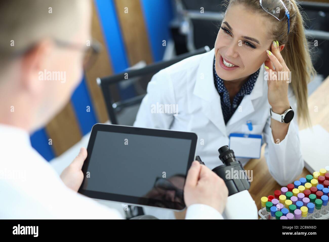 Female laborant sit on chait, examines biomaterial with microscope and ...