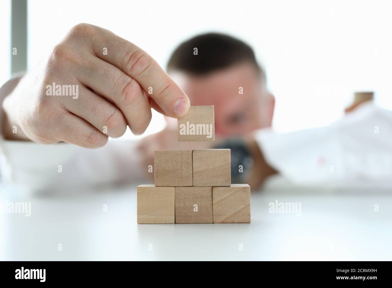 Man in shirt build tower of wooden cubes on table in office close up ...
