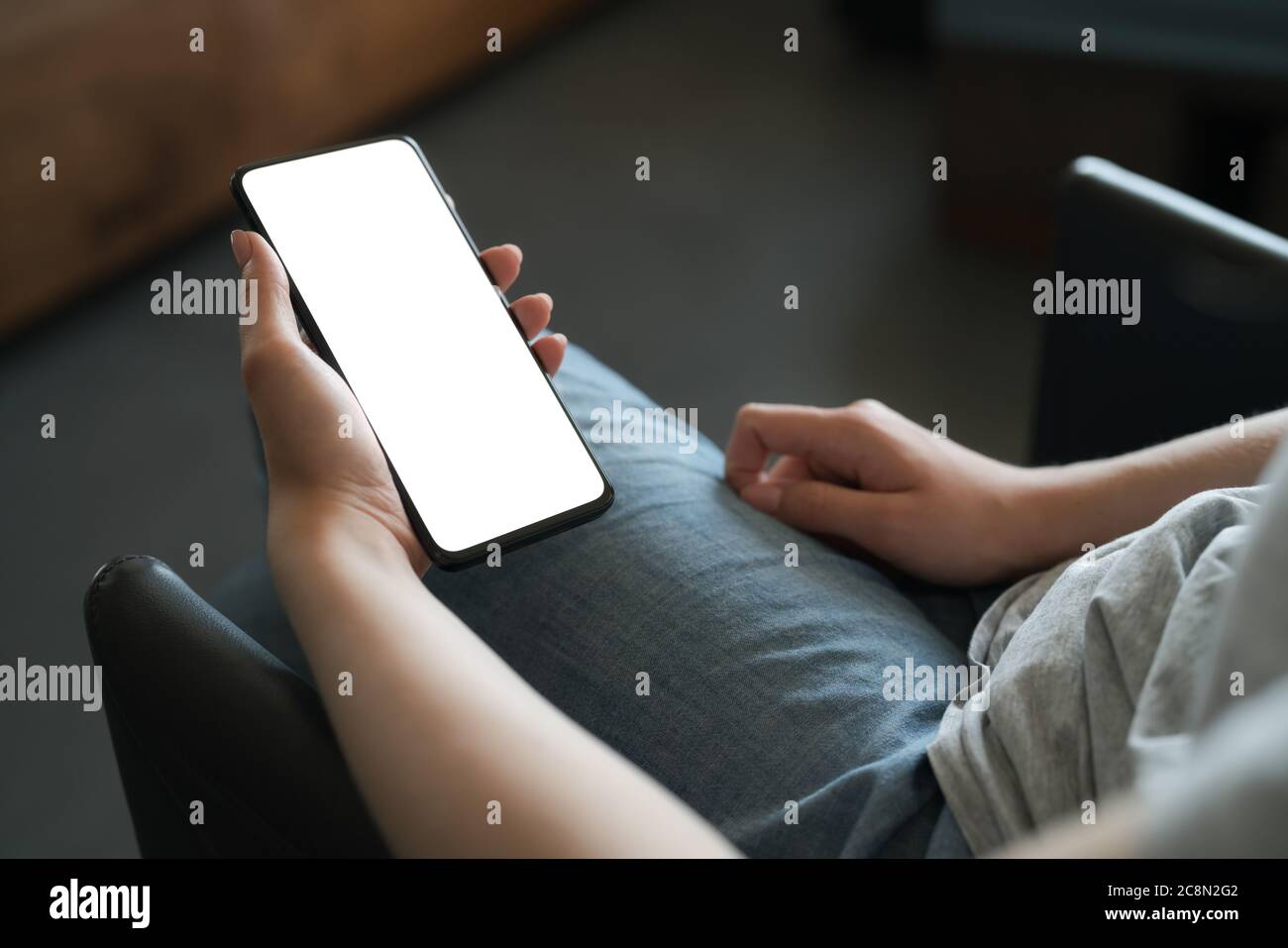 Young woman sitting in chair and holding smartphone with white screen ...