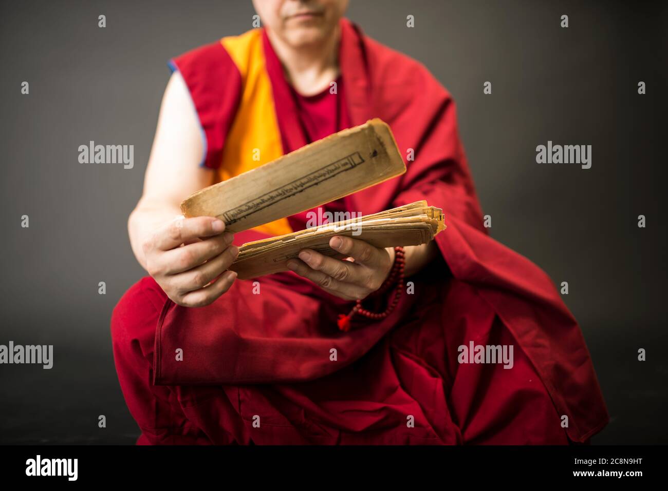 Buddhist monk in red dress holding prayer texts with mantras in his ...