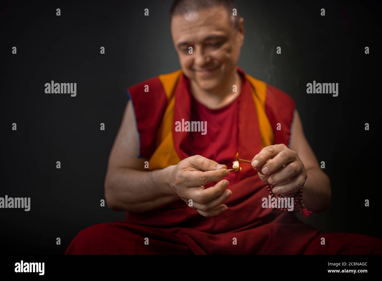 Buddhist monk in red kesa, holding an incense stick with incense in his ...