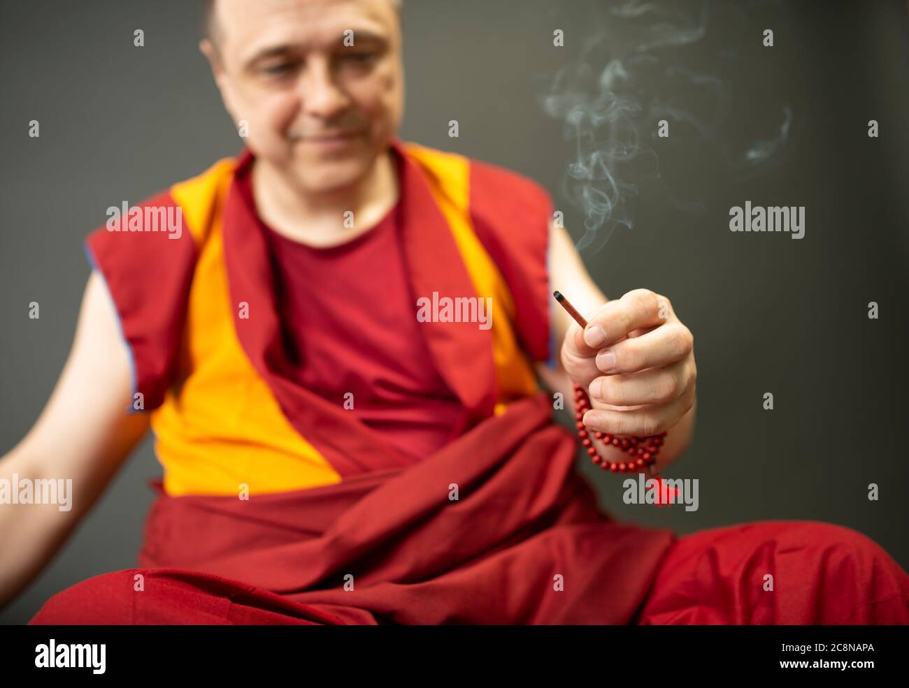 Buddhist monk in red kesa, holding an incense stick with incense in his ...