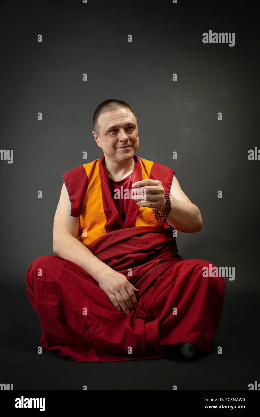 Buddhist monk in red kesa, holding an incense stick with incense in his ...