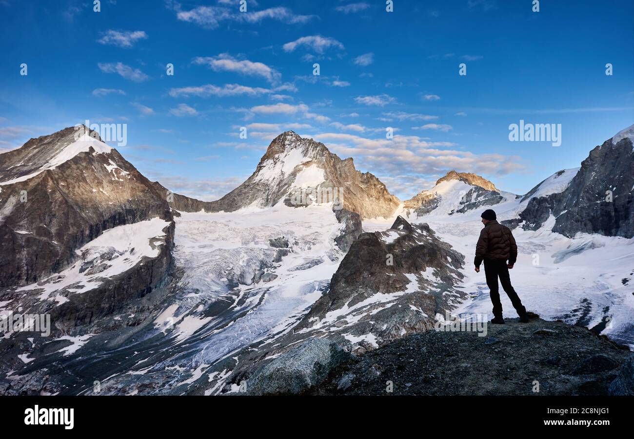Man tourist welcoming new day in the Swiss Alps, morning bright sun is ...