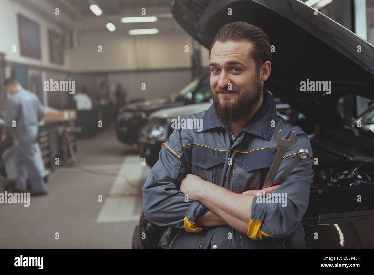 Cheerful bearded mechanic in grey uniform smiling to the camera ...
