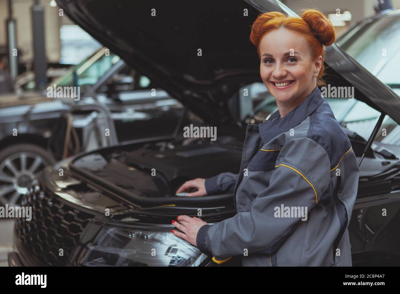 Lovely female mechanic smiling to the camera over her shoulder, while ...