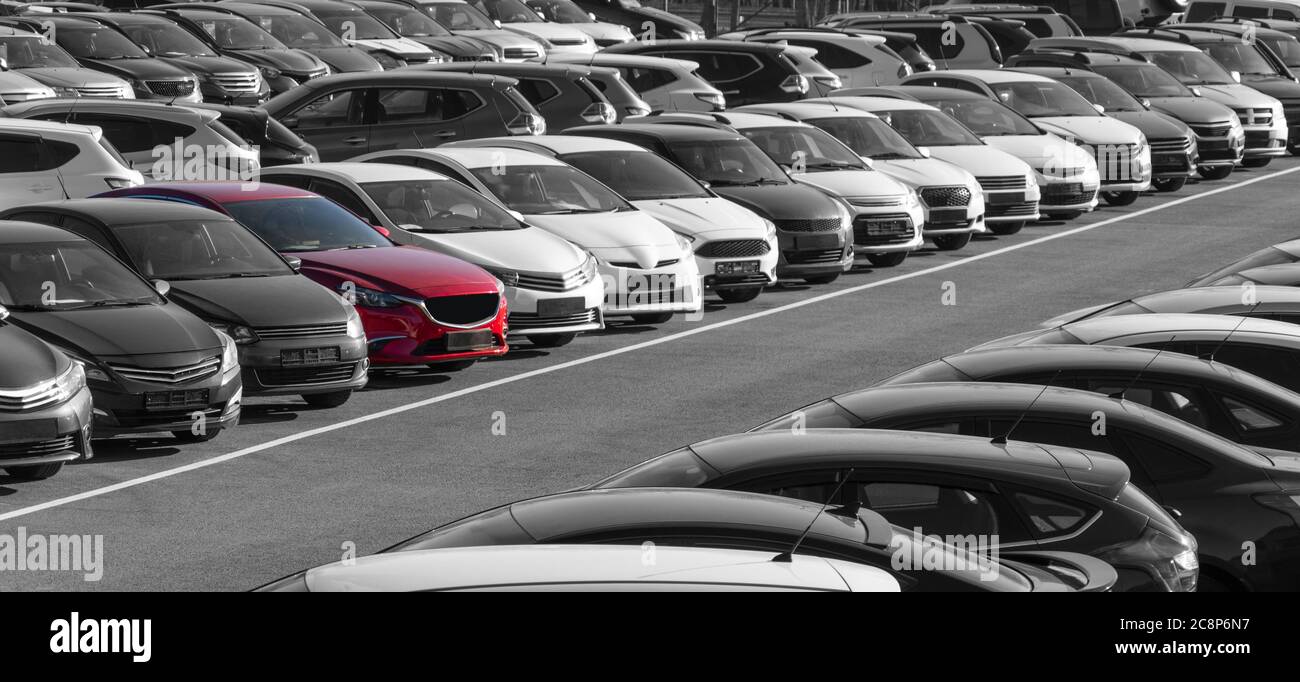 Black and white image of a row of cars. Only the red car has color ...