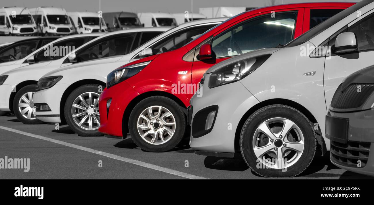 Black and white image of a row of cars. Only the red car has color ...