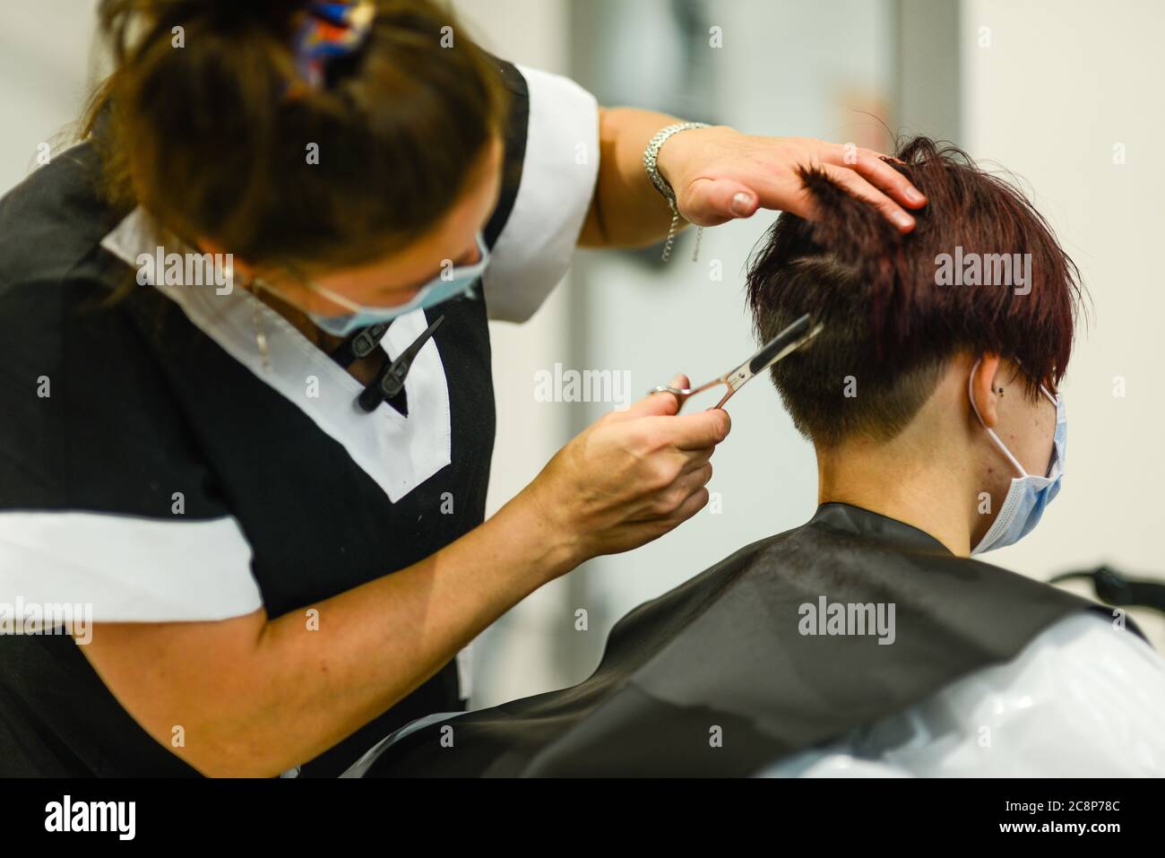Hair stylist wearing face mask cutting and styling the hair of a dark ...