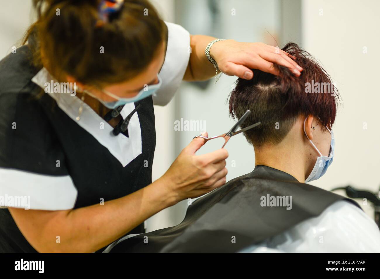 Hair stylist wearing face mask cutting and styling the hair of a dark ...