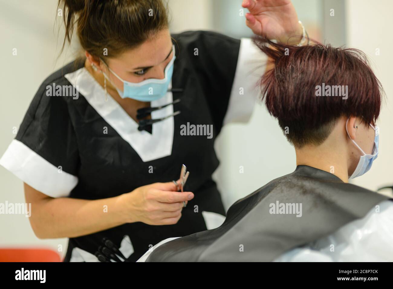 Hair stylist wearing face mask cutting and styling the hair of a dark ...