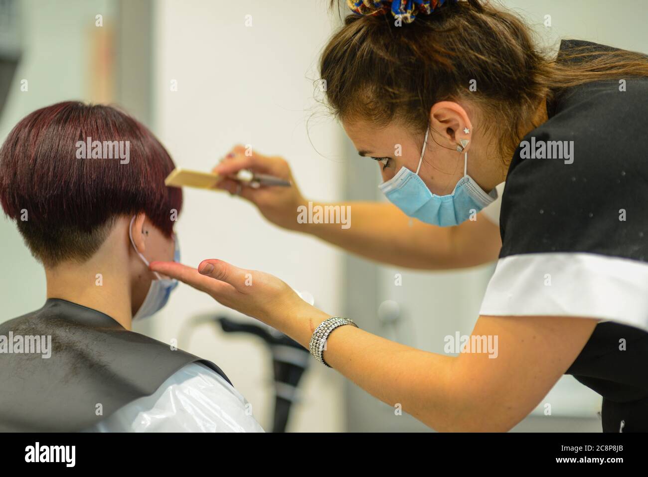 Hair stylist wearing face mask cutting, combing and styling the hair of ...